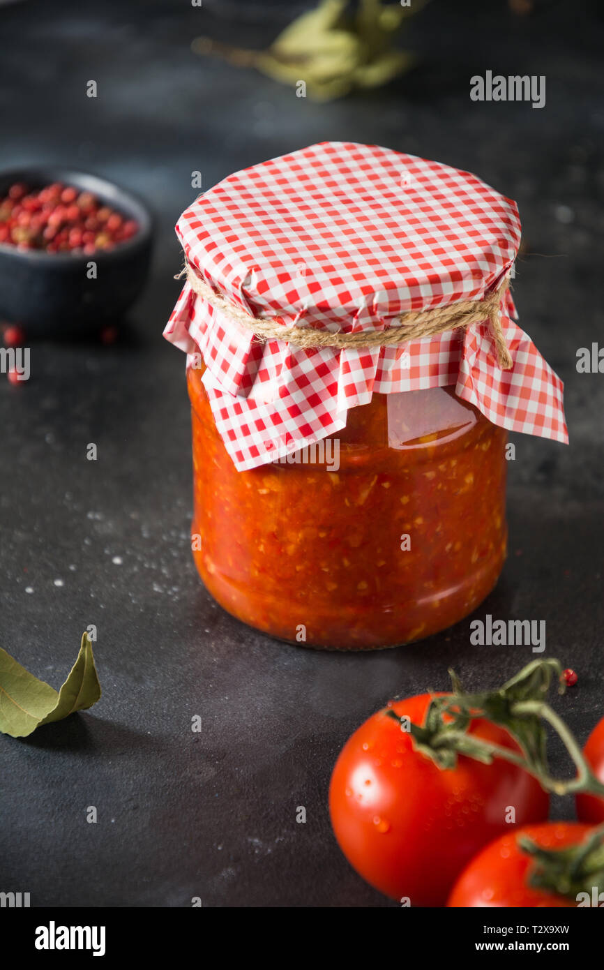Homemade adjika with tomatoes in jar on black background. Close-up ...
