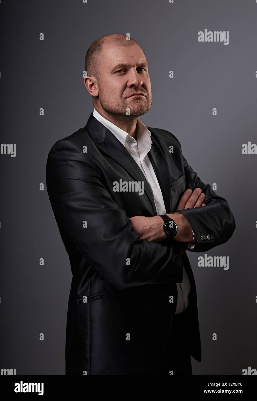 Serious bald thinking business man with folded arms in suit on grey ...