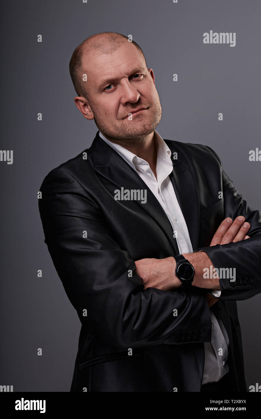 Serious bald business man with folded arms in suit on grey background ...