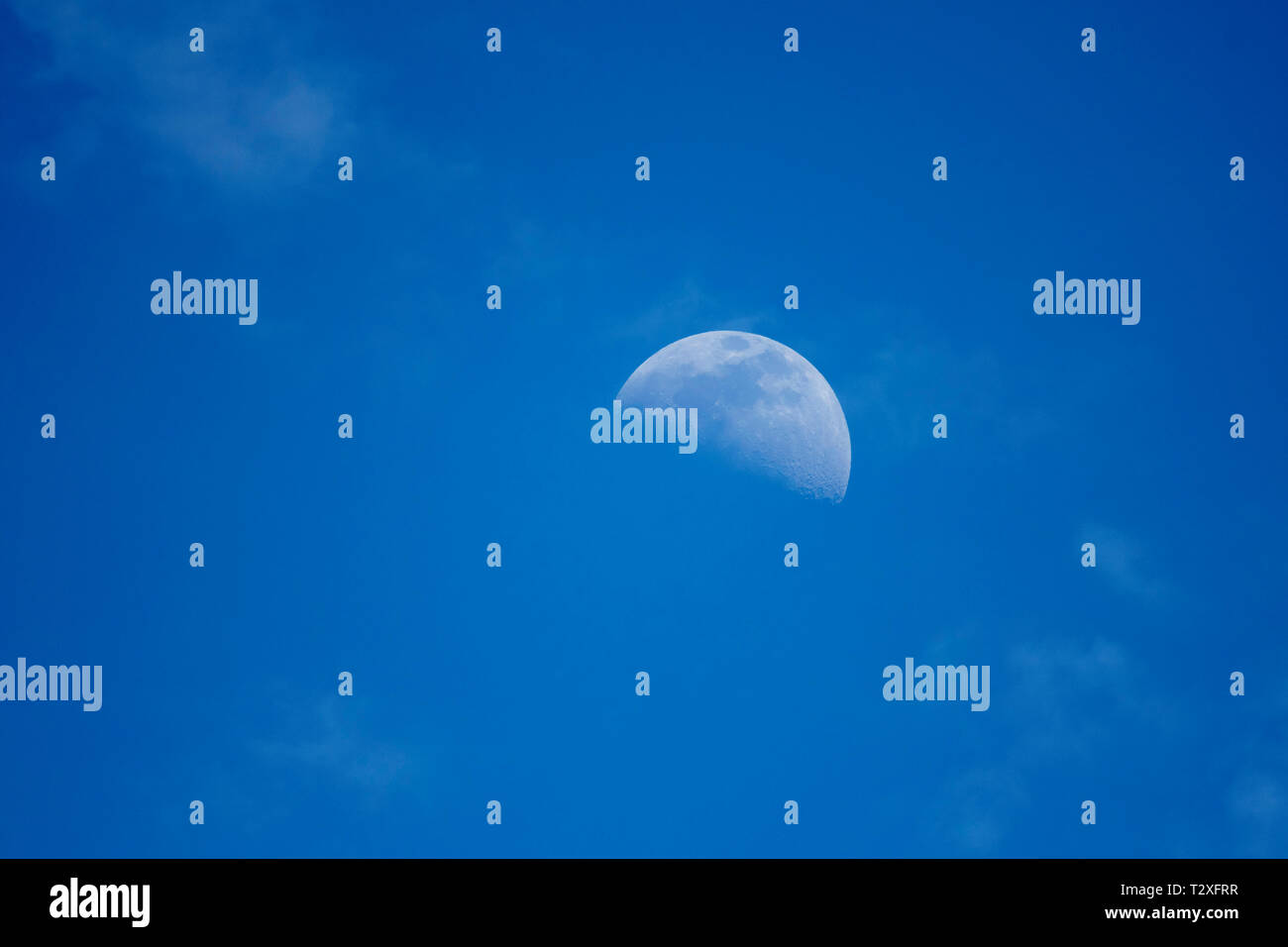 A half moon in the daytime sky with a diagonal pattern of wispy clouds ...