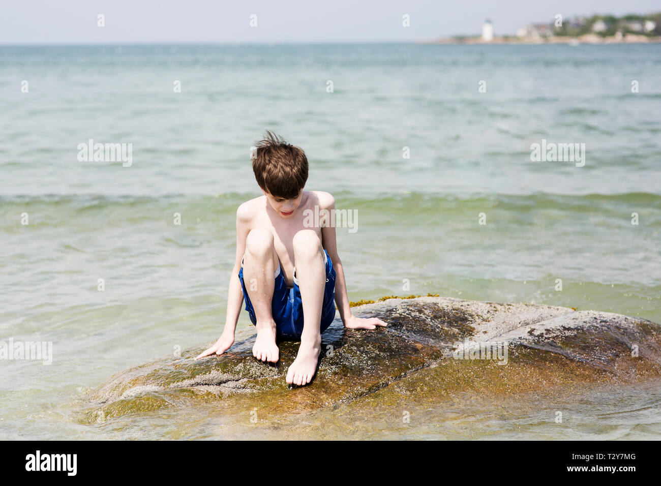 A twelve year old boy sitting on the rocks as the tide comes in at ...