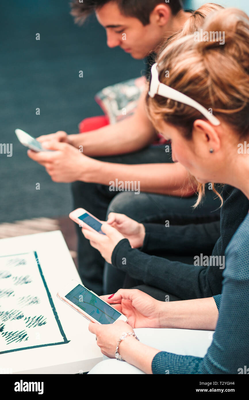Family members using mobile phones together, sitting on sofa in lounge ...