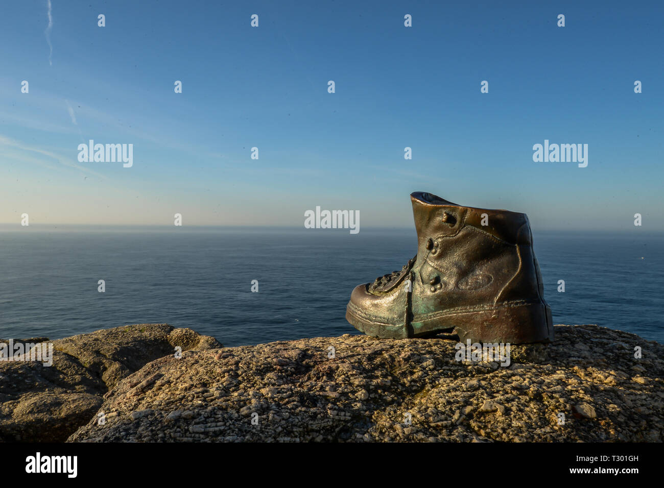 A cast bronze boot on the rocks at the end of camino de santiago ...