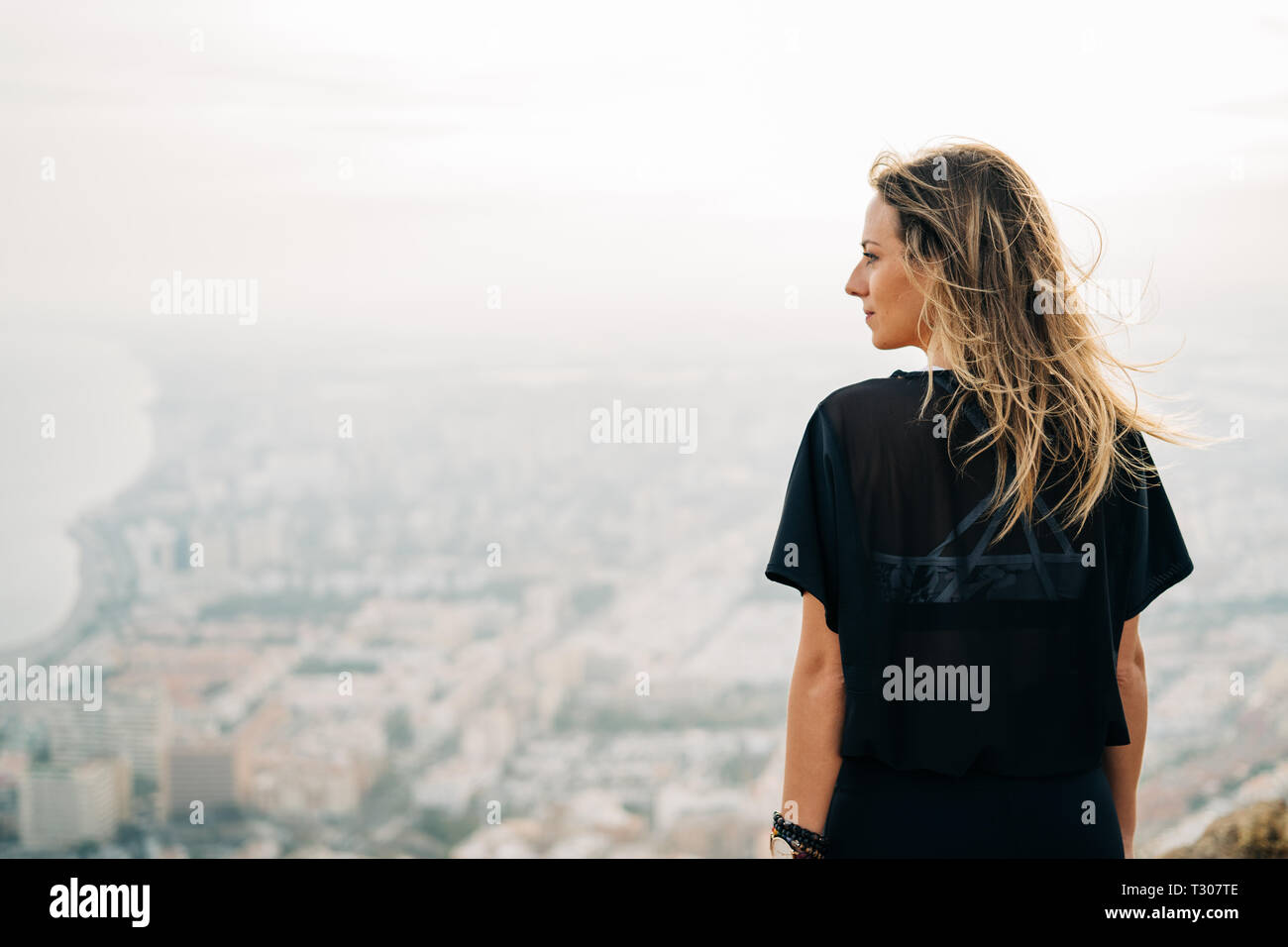 Young beautiful woman on top of the mountain looking at the city from ...