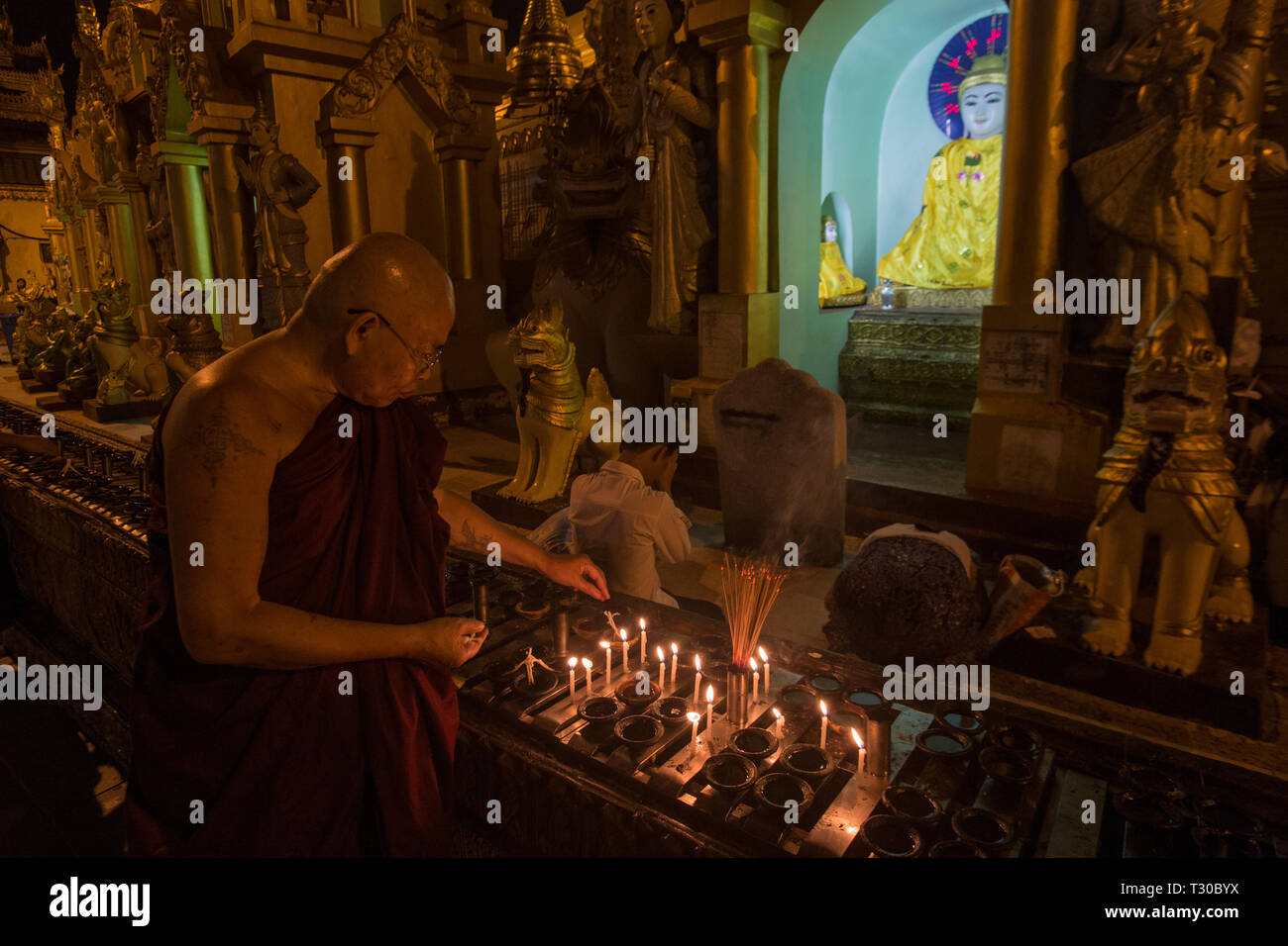 Burmese Buddhist monk lighting oil lamps at the Shwedagon Pagoda ...