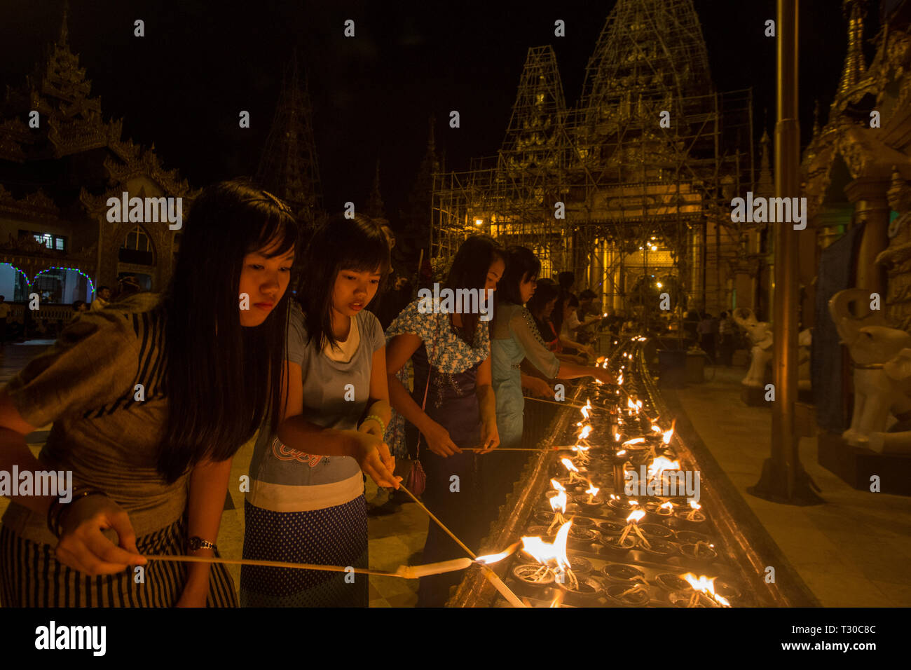 Burmese Buddhist devotees lighting oil lamps at the Shwedagon Pagoda ...