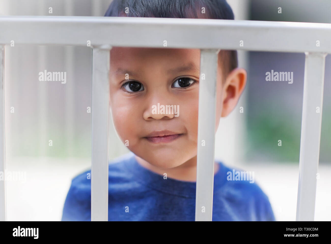Young hispanic boy behind bars from a crib looking sad about getting a ...