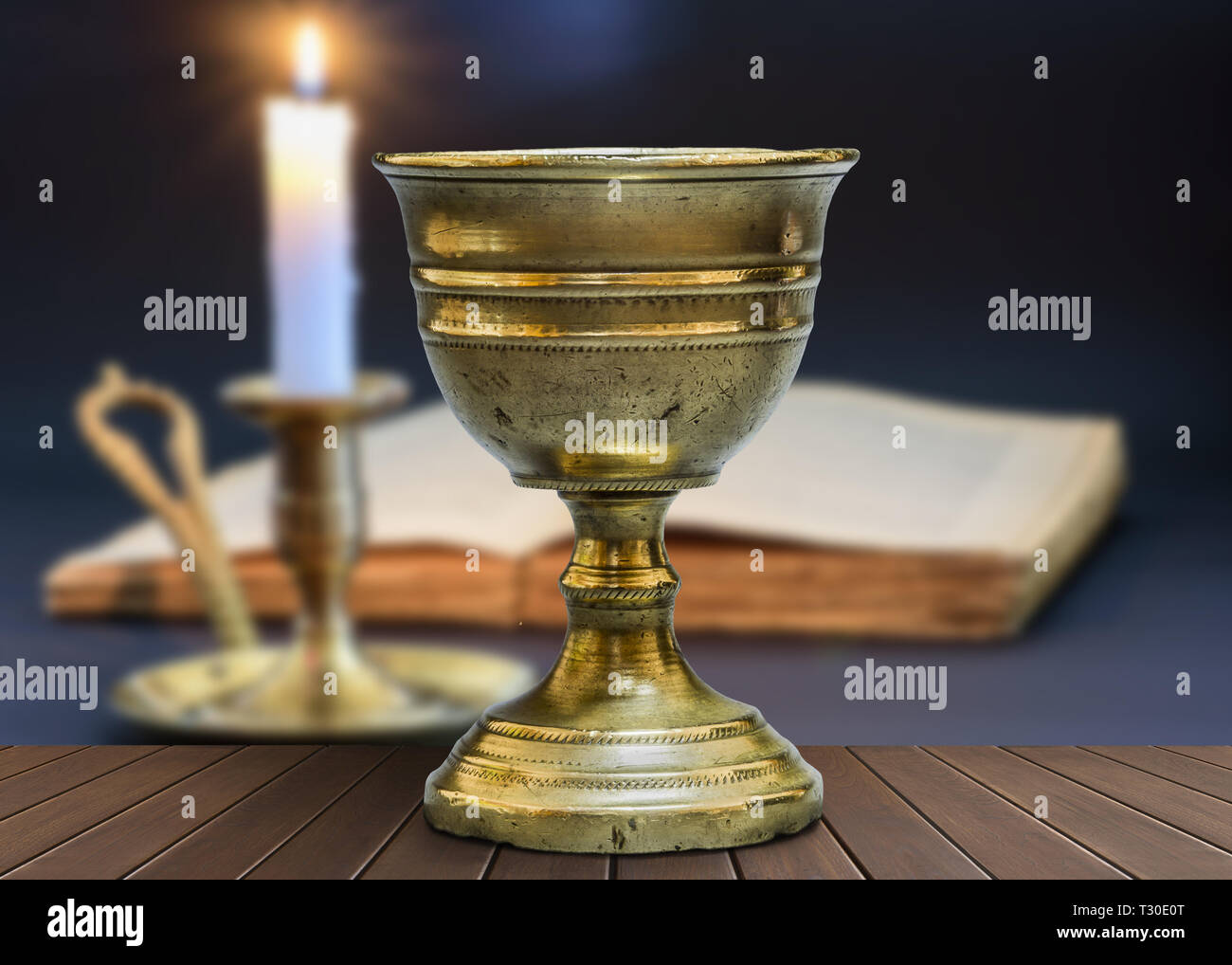 Old chalice on wooden table next to a candle and an open book Stock ...