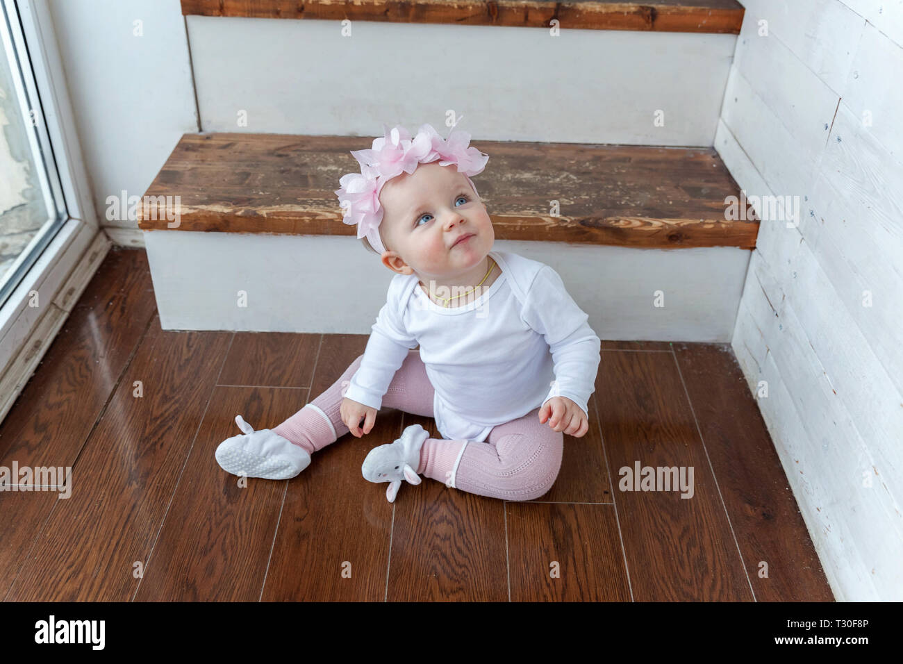 Little crawling baby girl one year old siting on floor in bright light ...