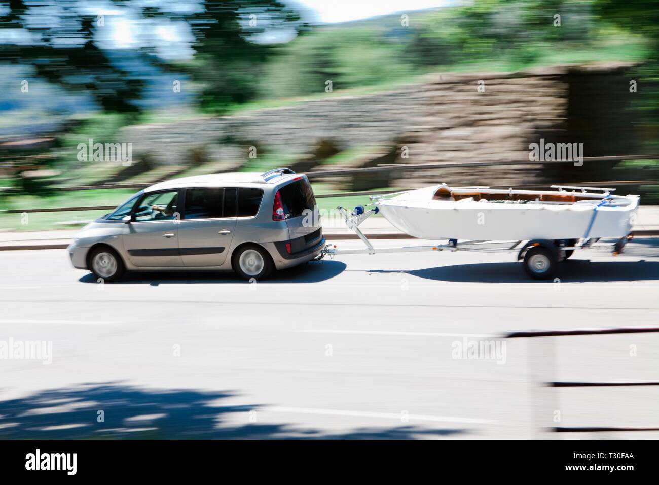 Silver family car is pulling white boat during summer day, going on ...