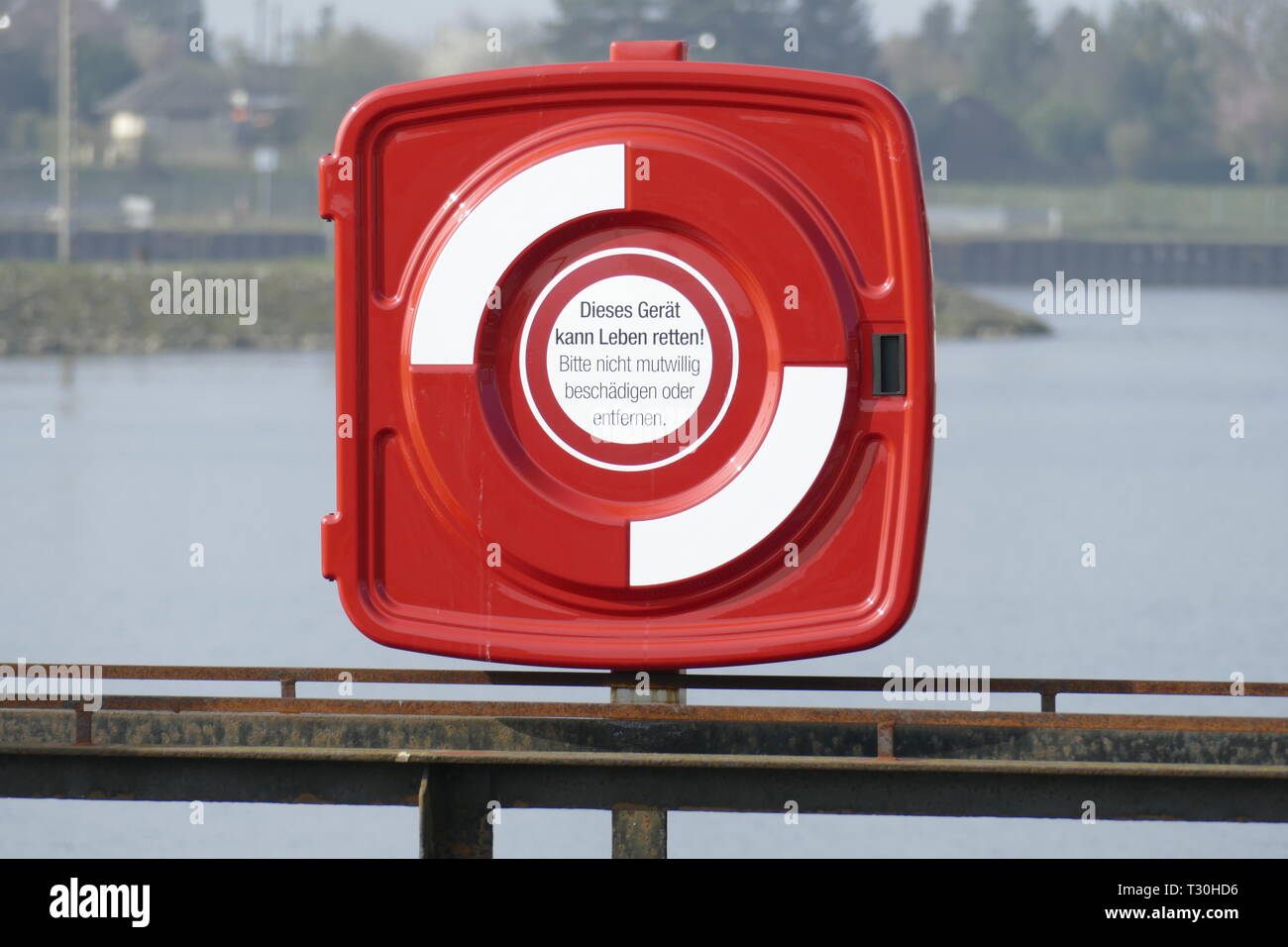 Red lifebuoy in a container on a railing at a body of water Stock Photo ...