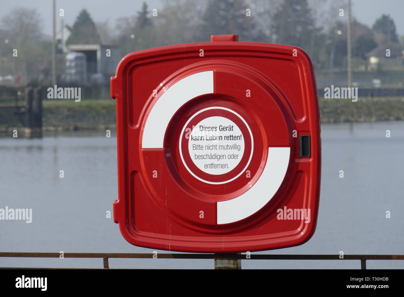 Red lifebuoy in a container on a railing at a body of water Stock Photo ...