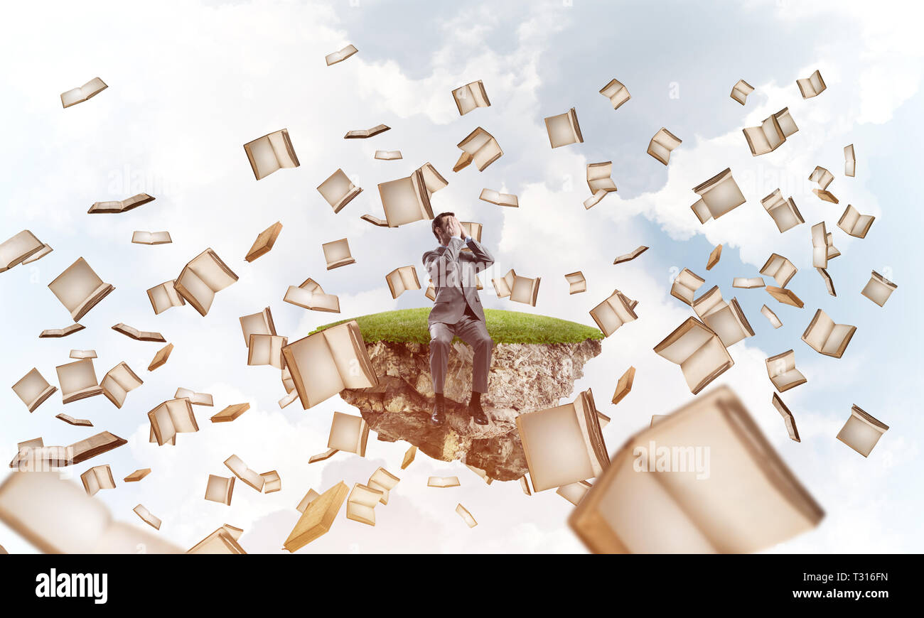 Young shocked businessman sitting on floating island and covering eyes ...