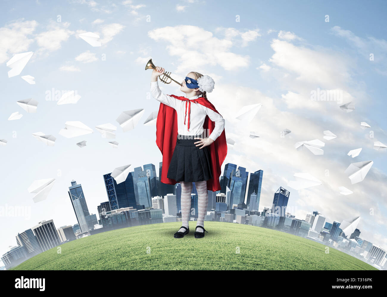 Little confident child in mask and cape plays trumpet against sunset ...