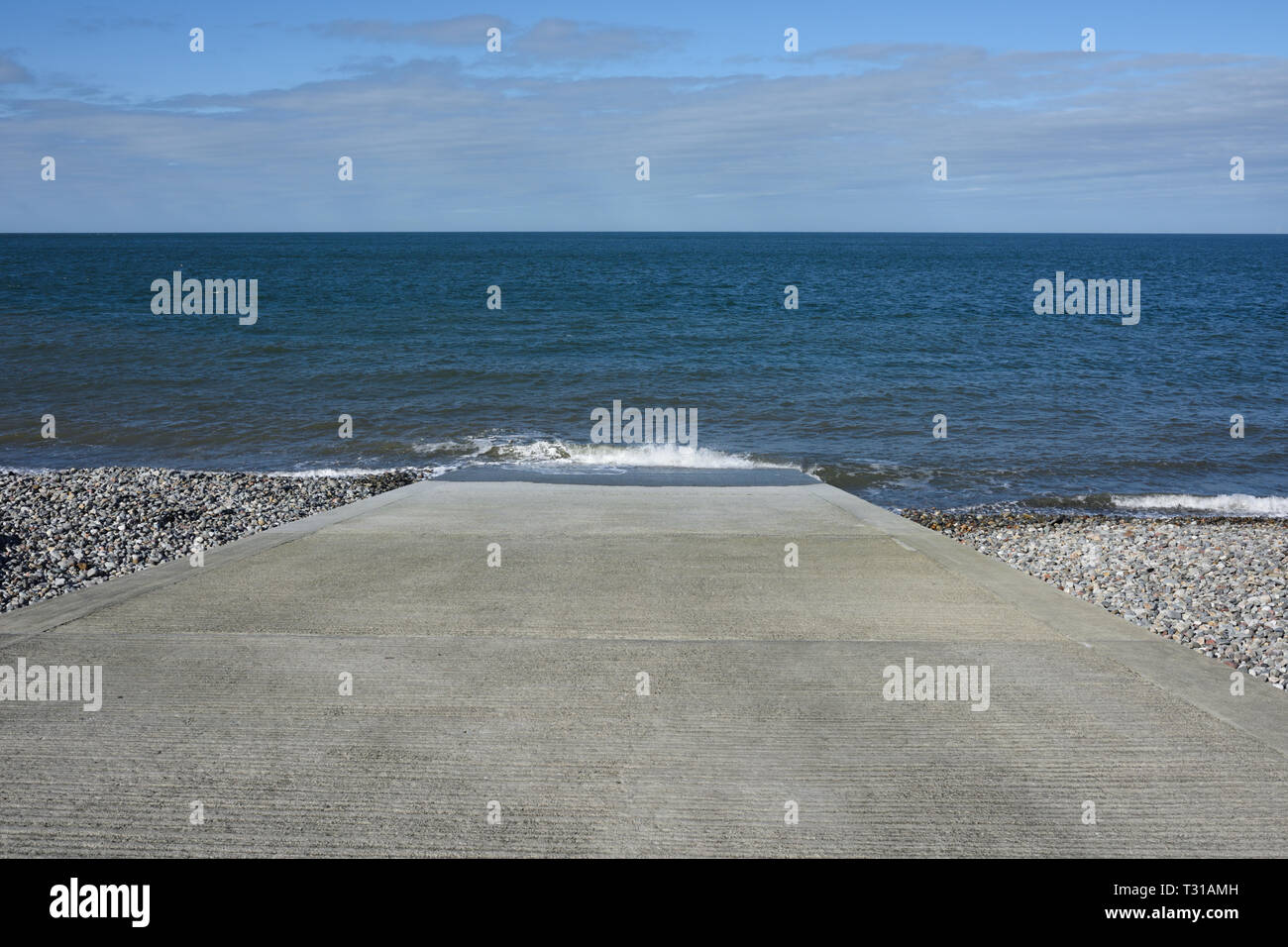 Concrete slipway on shingle beach with calm sea and horizon in ...