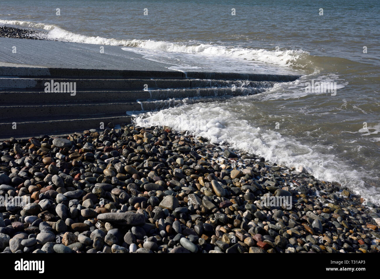 Concrete steps on side of slipway with sea lapping at base and onto ...