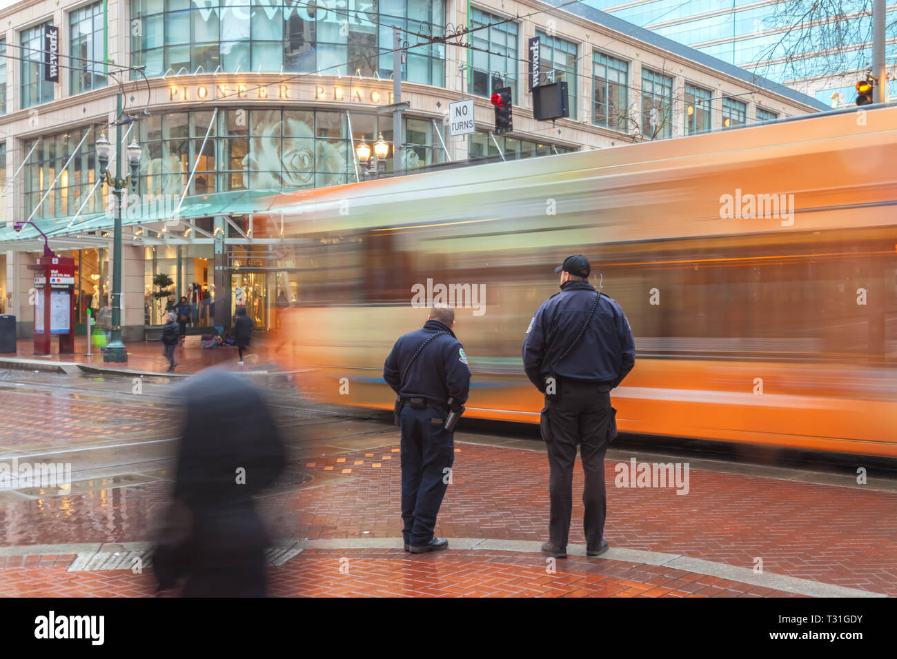 Two police officers stand at the intersection, with a moving bus in ...