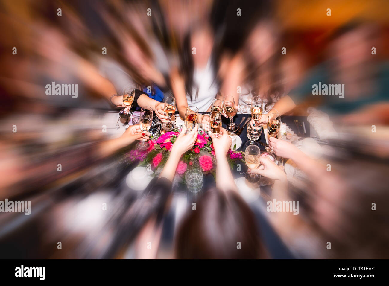 Defocused blur of group of unknown girls with raised glasses toasting ...