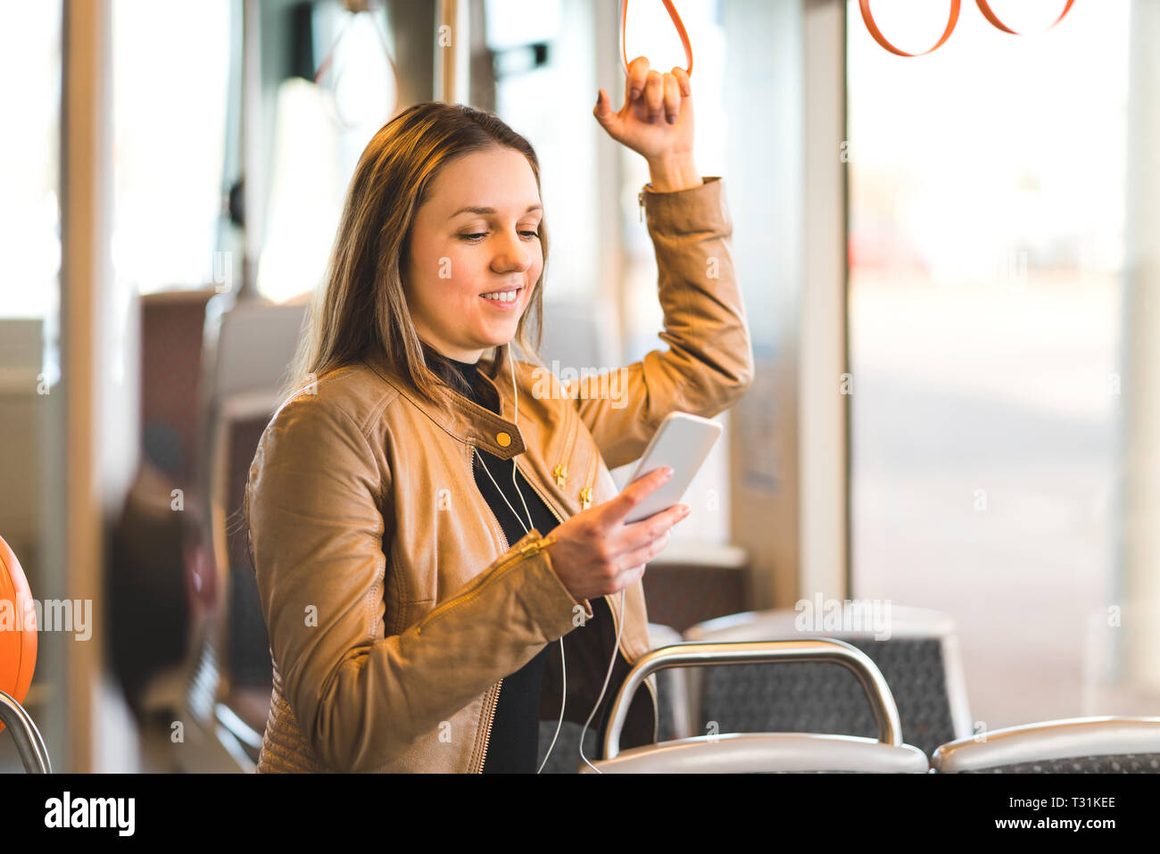 Woman standing in train, tram or bus holding the handle and using ...