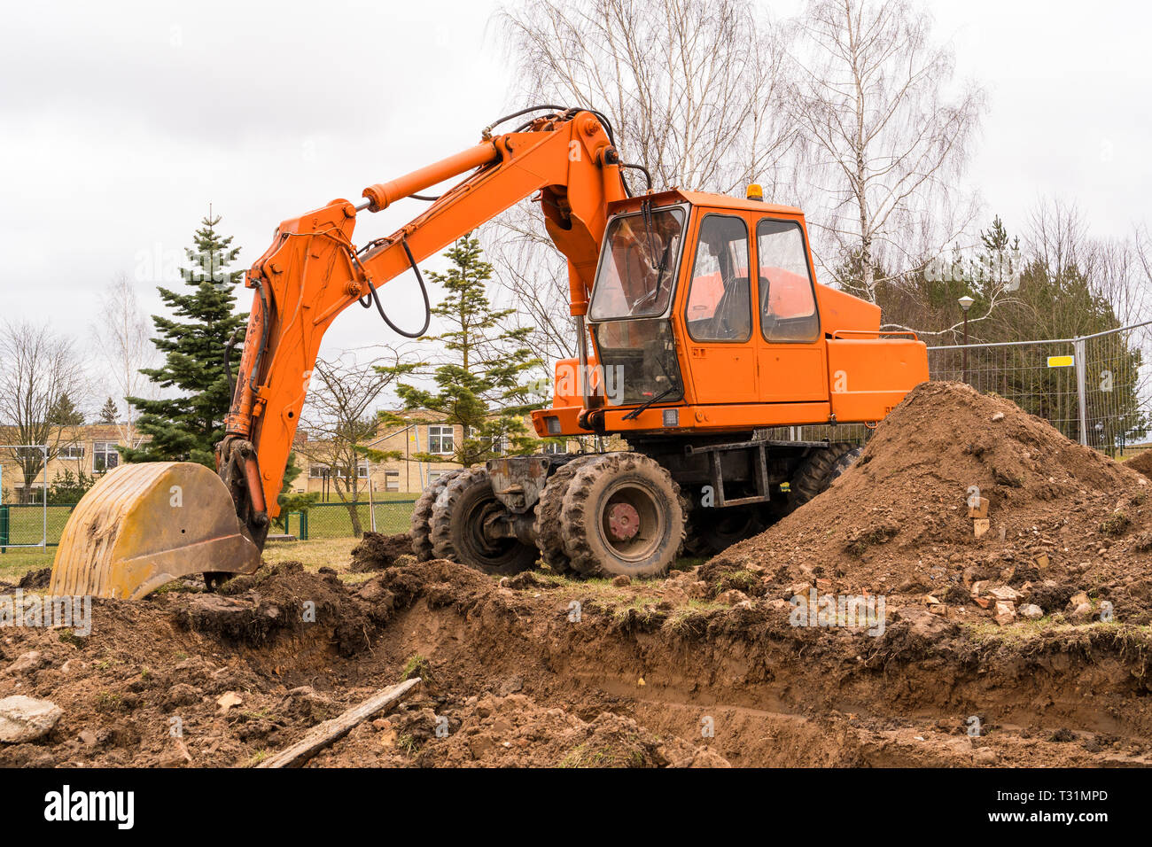 An orange excavator digging a trench for city communications Stock ...