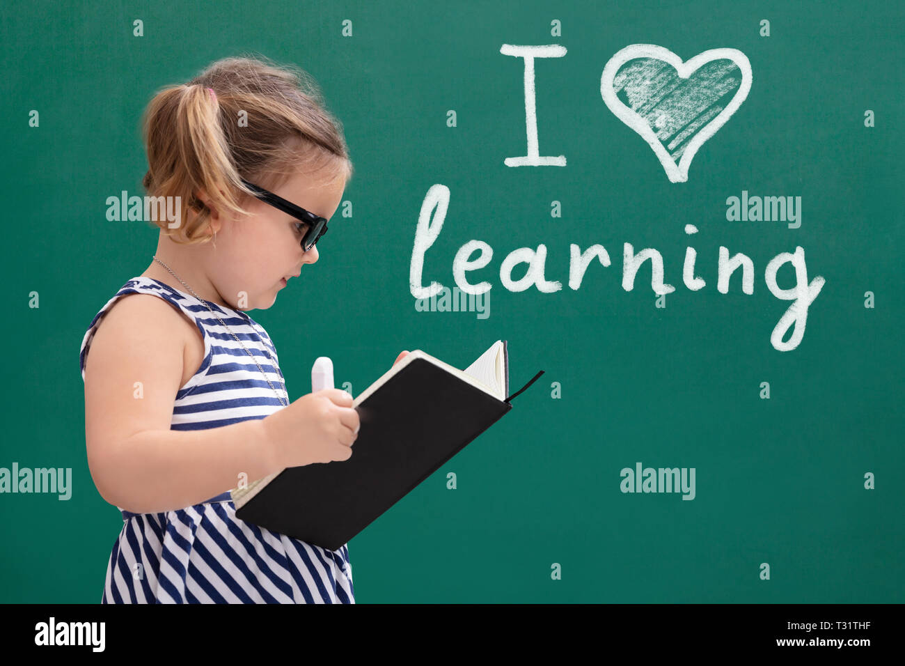 Little Girl Standing In Front Of Chalkboard Reading Book With Learning ...