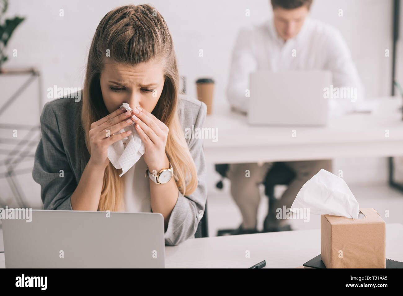 blonde businesswoman sneezing in tissue near coworker in office Stock ...