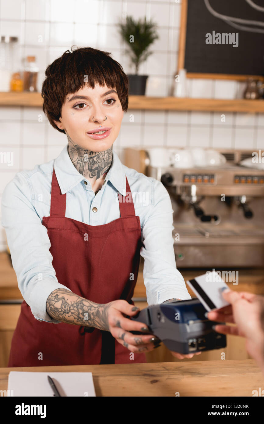 smiling cashier holding payment terminal near buyer with credit card ...