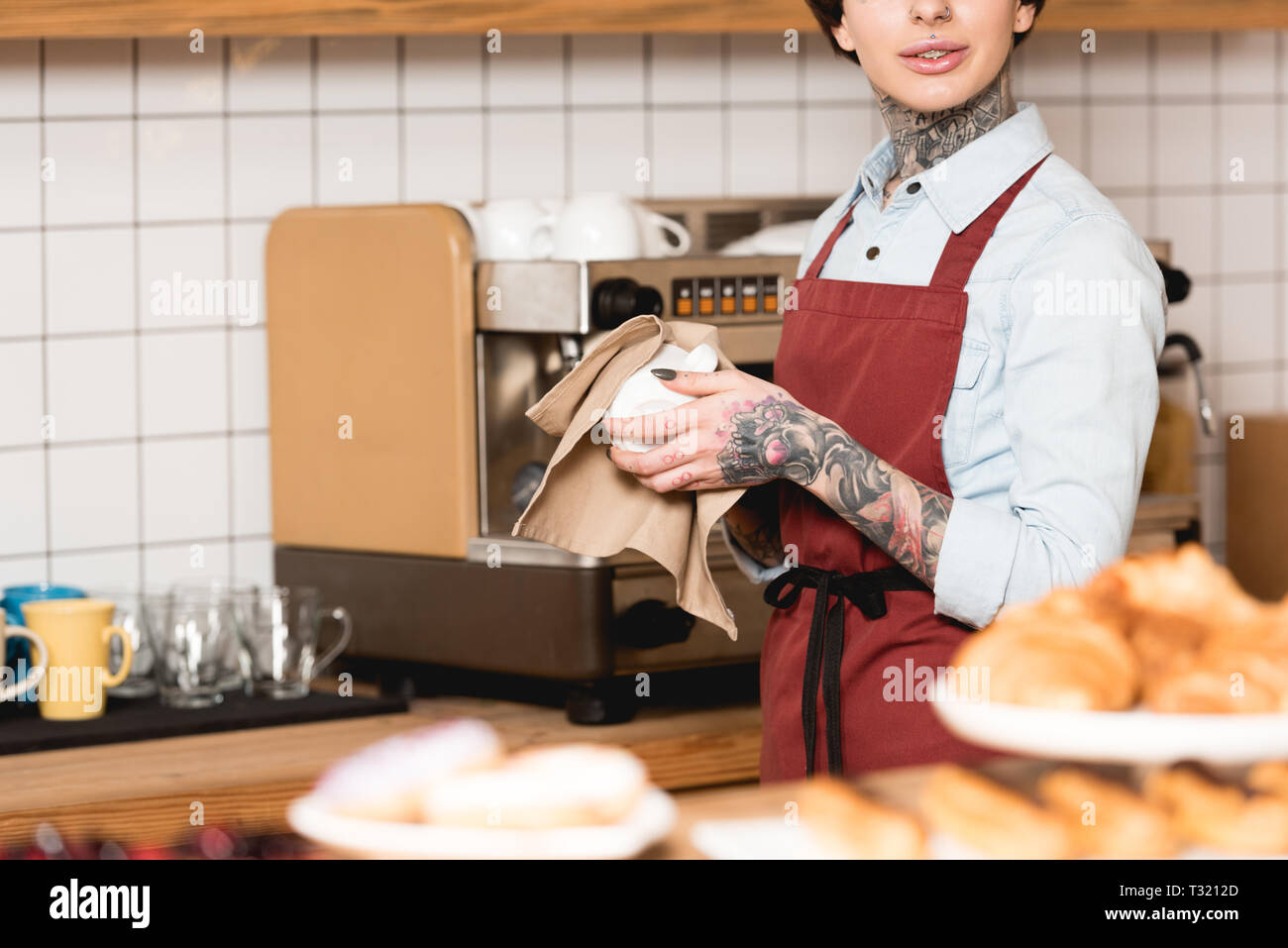 partial view of barista wiping cup while standing near coffee machine ...