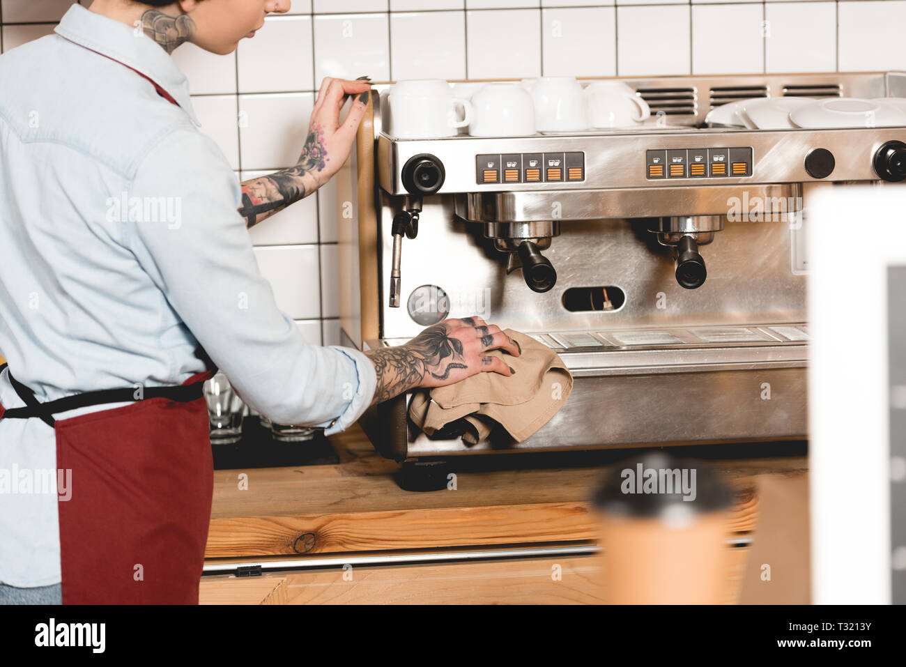 partial view of barista wiping espresso machine with rag in coffee shop ...