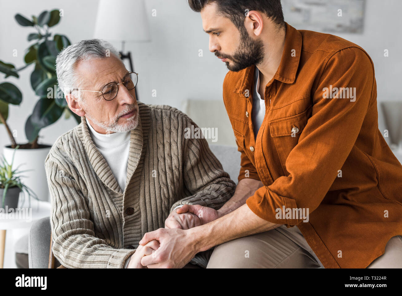 senior father in glasses and handsome son holding hands at home Stock ...