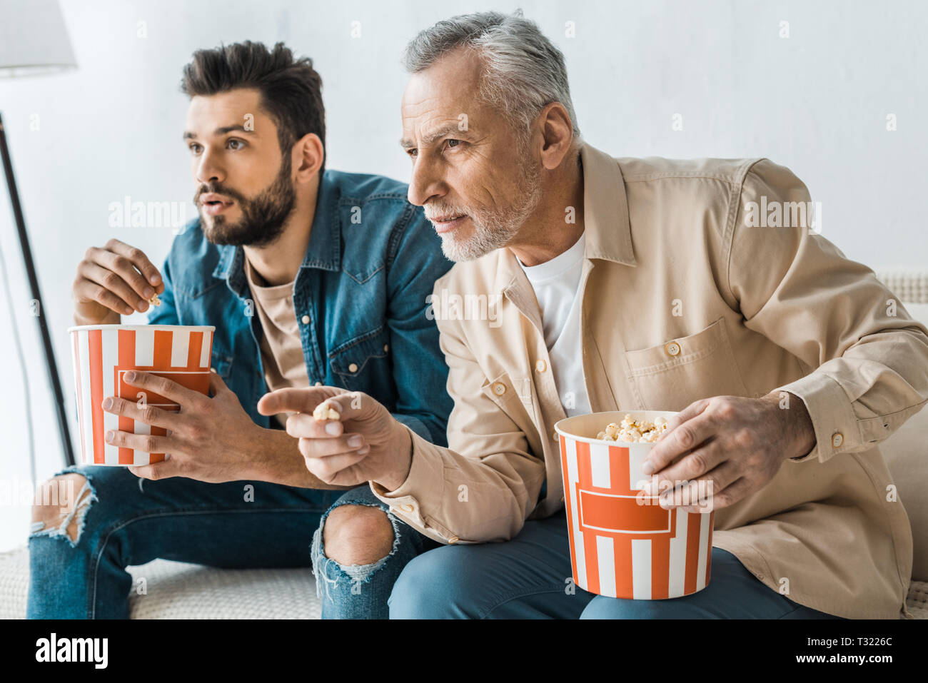 senior father pointing with finger near handsome son with popcorn ...