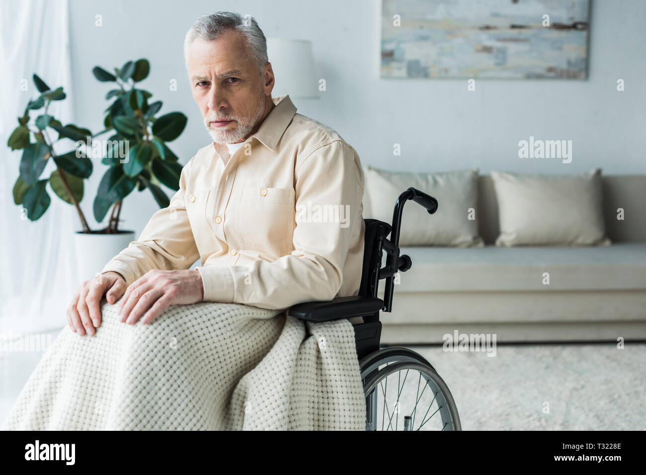 sad disabled retired man sitting in wheelchair and looking at camera ...