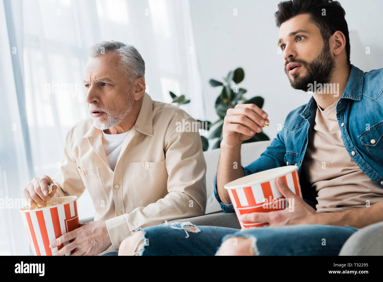 Shocked Senior Father Sitting With Son And Holding Popcorn Bucket While