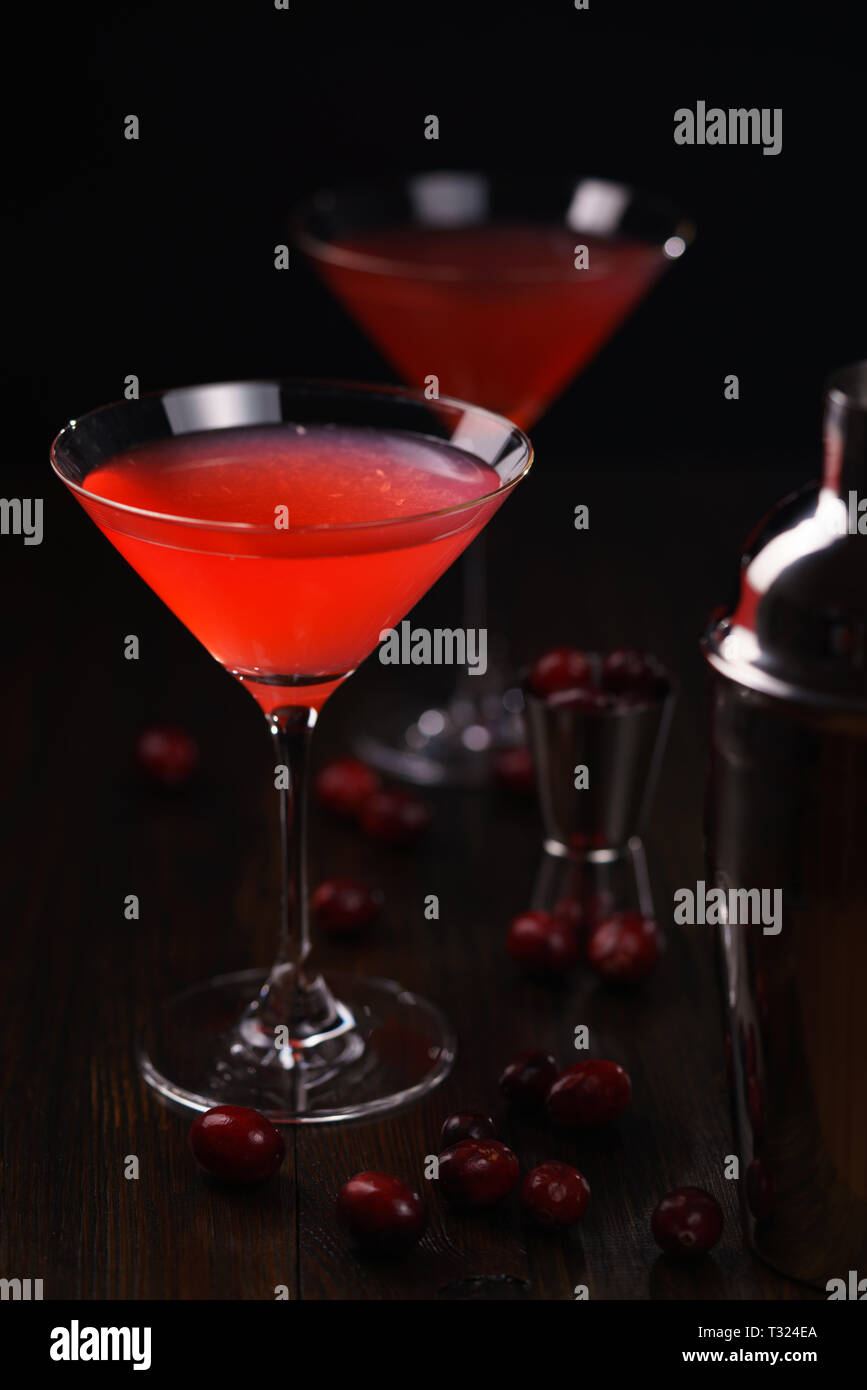 Cosmopolitan cocktail with cranberries, shaker and jigger. Dark wooden ...