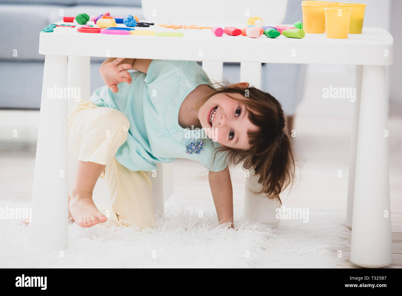 Little cute girl crawled under the table. The kid smiles, plays hide ...
