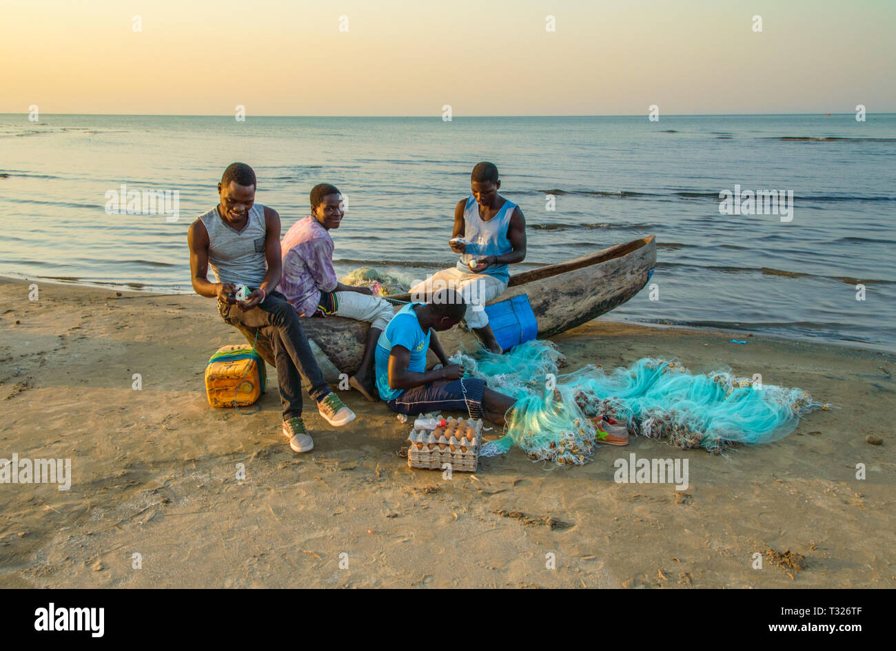 Four Malawian men sit in a fishing canoe eating a meal of boiled eggs ...