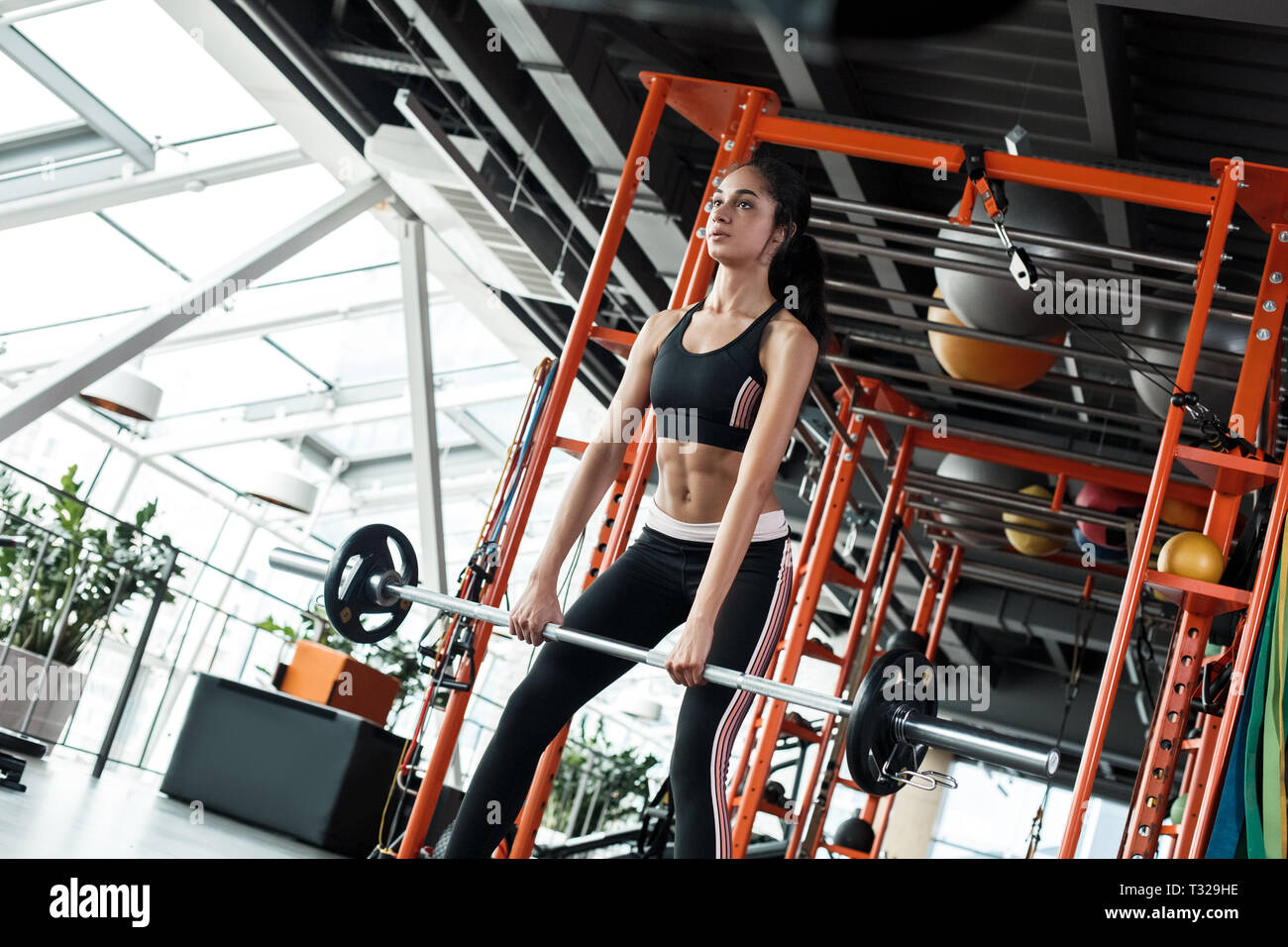 Young girl in gym sporty lifestyle concept standing lifting barbell ...