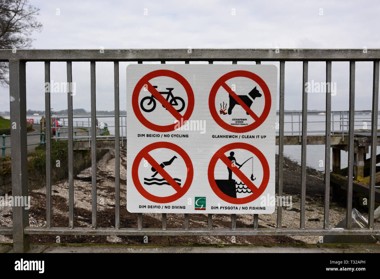 Red on white warning sign on galvanized steel fence overlooking estuary ...