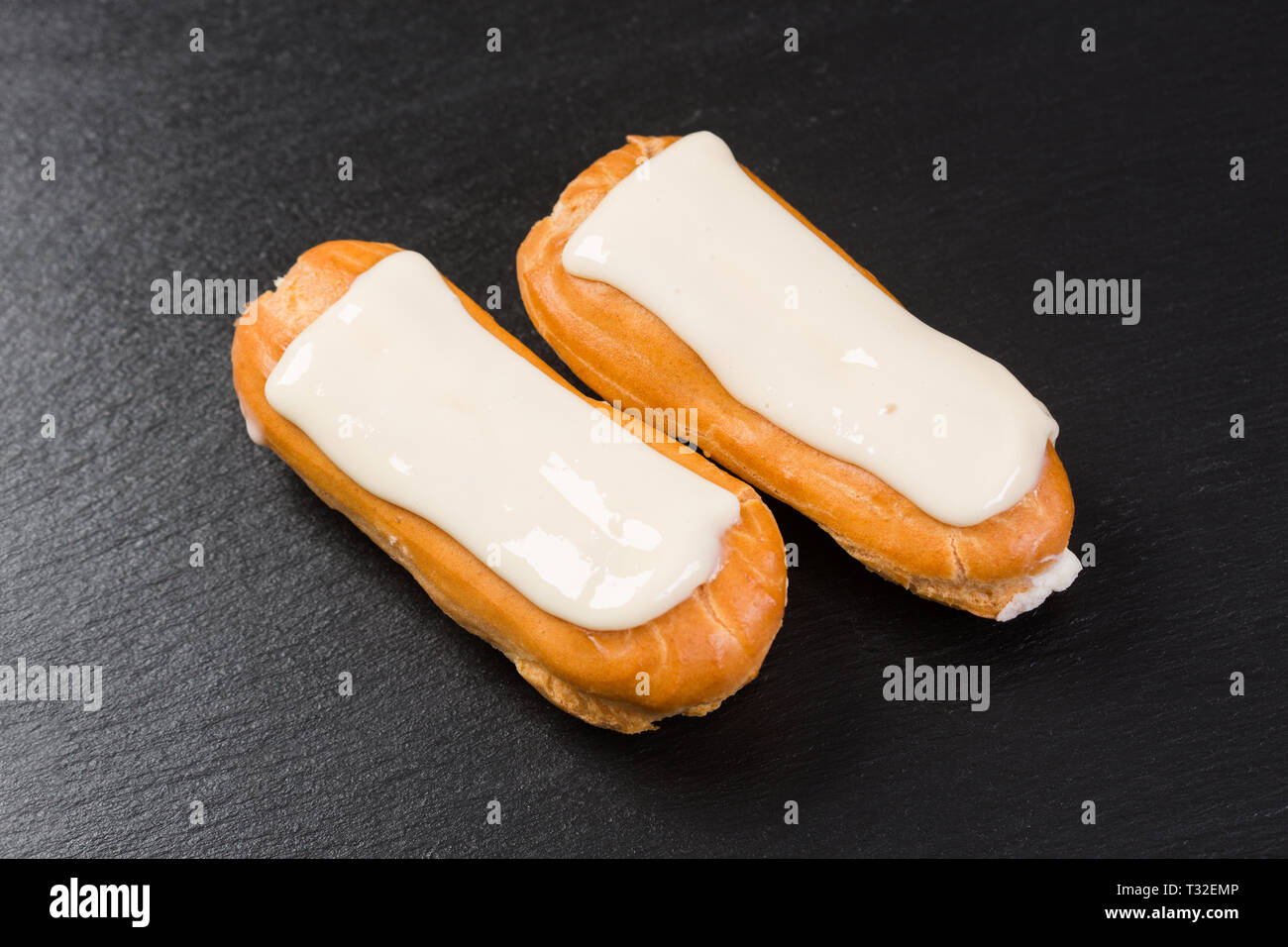Two eclairs with white icing on black background Stock Photo - Alamy