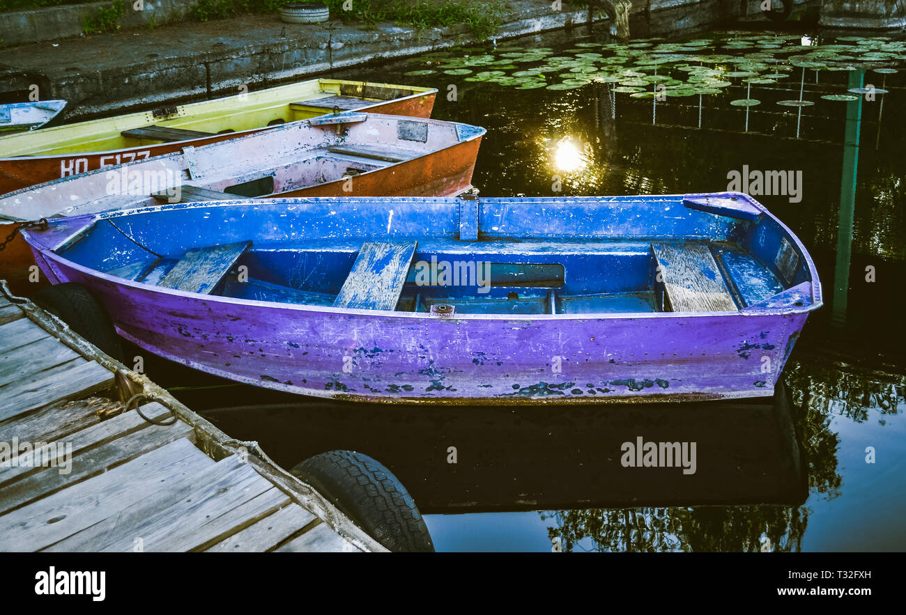 A few old shabby and worn boats different colors on the dock pier close ...
