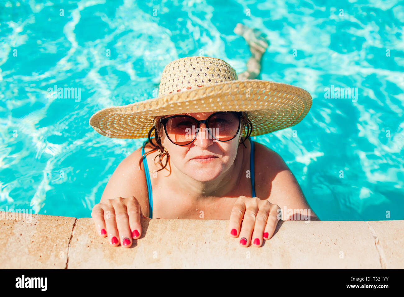 Senior woman in bikini relaxing in hotel swimming pool. People enjoying ...
