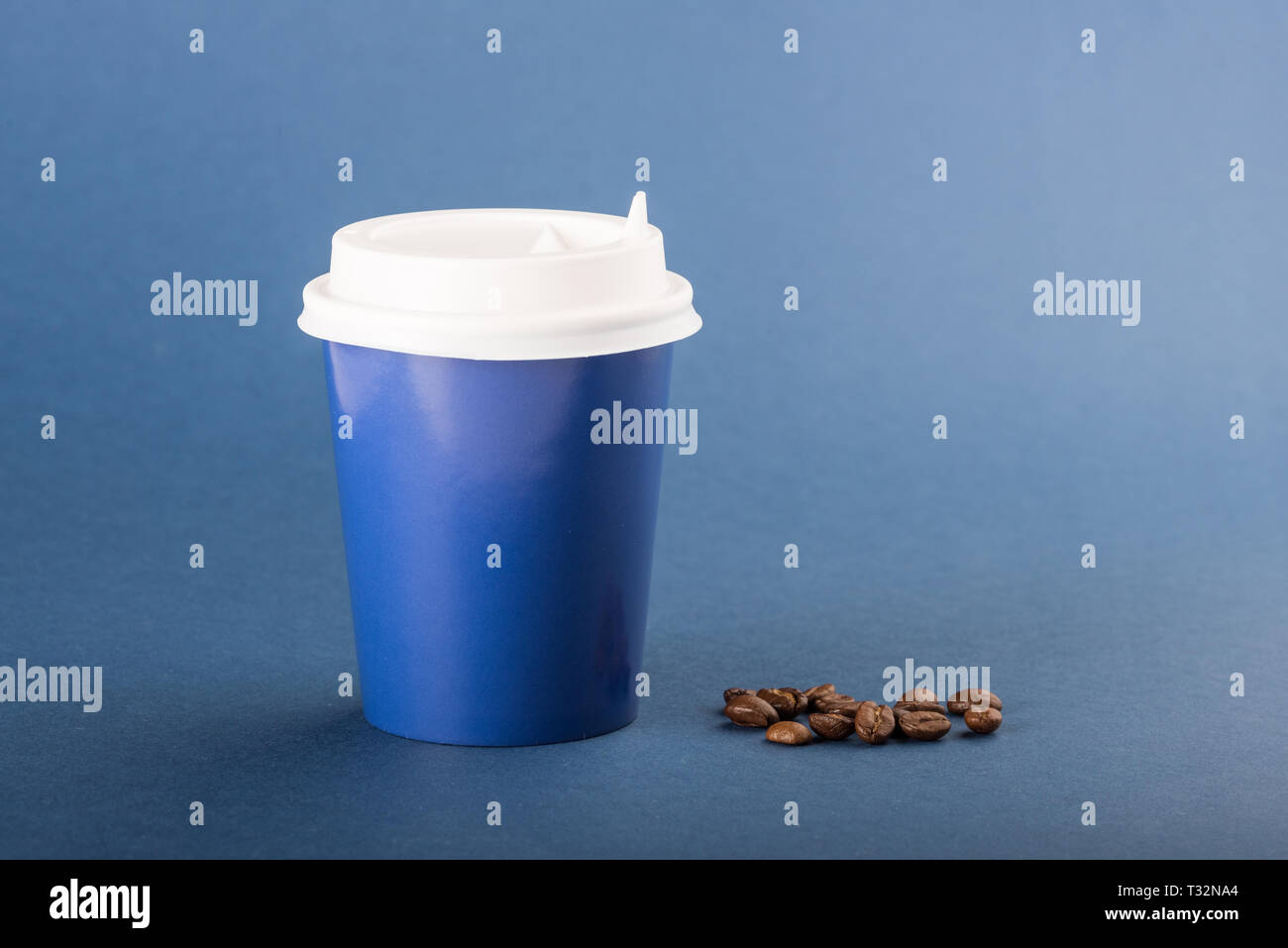 Blue disposable cup with white cap and coffee beans on a blue ...
