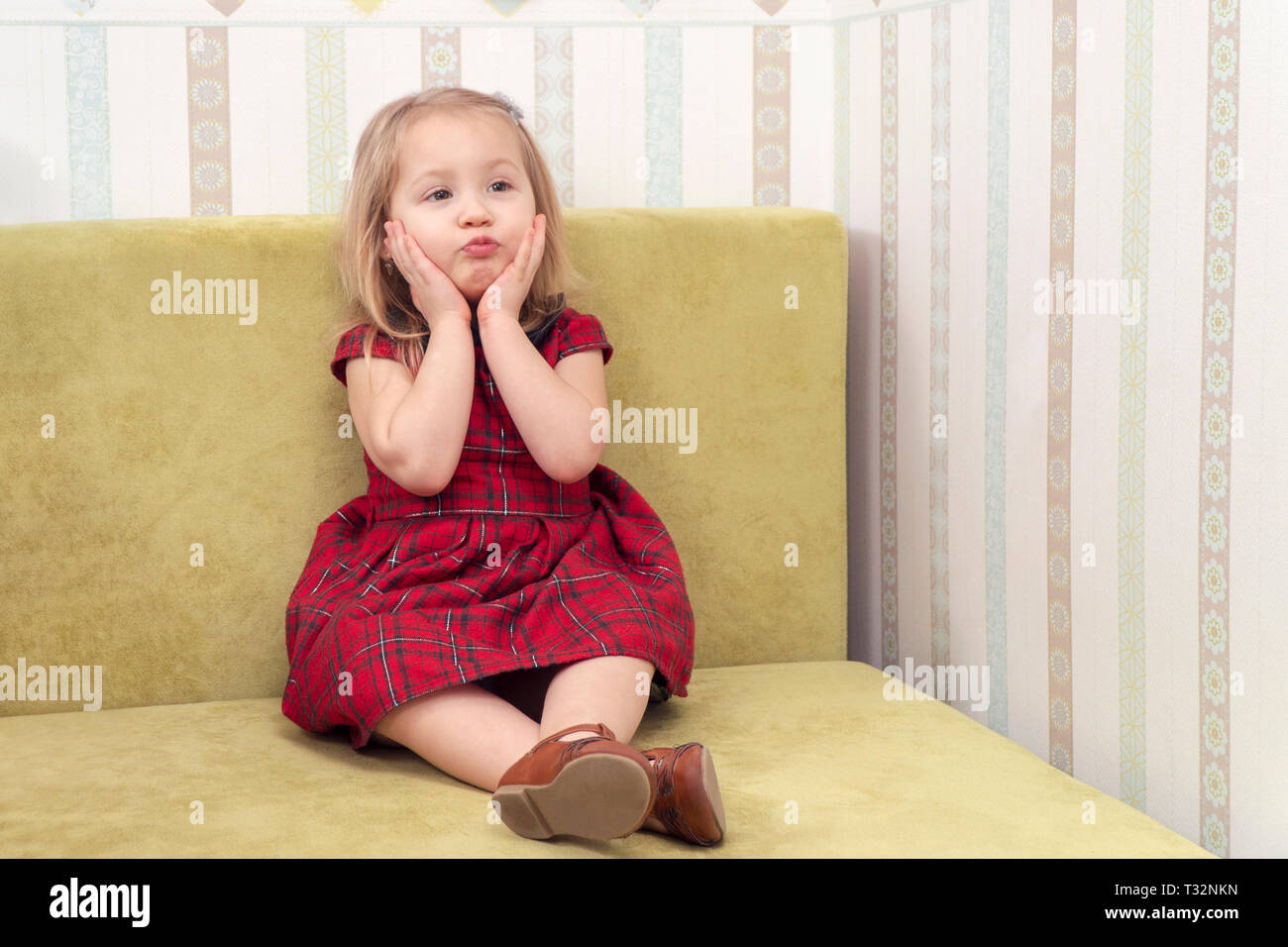 little girl sitting on the couch and holding on to his inflated cheeks ...