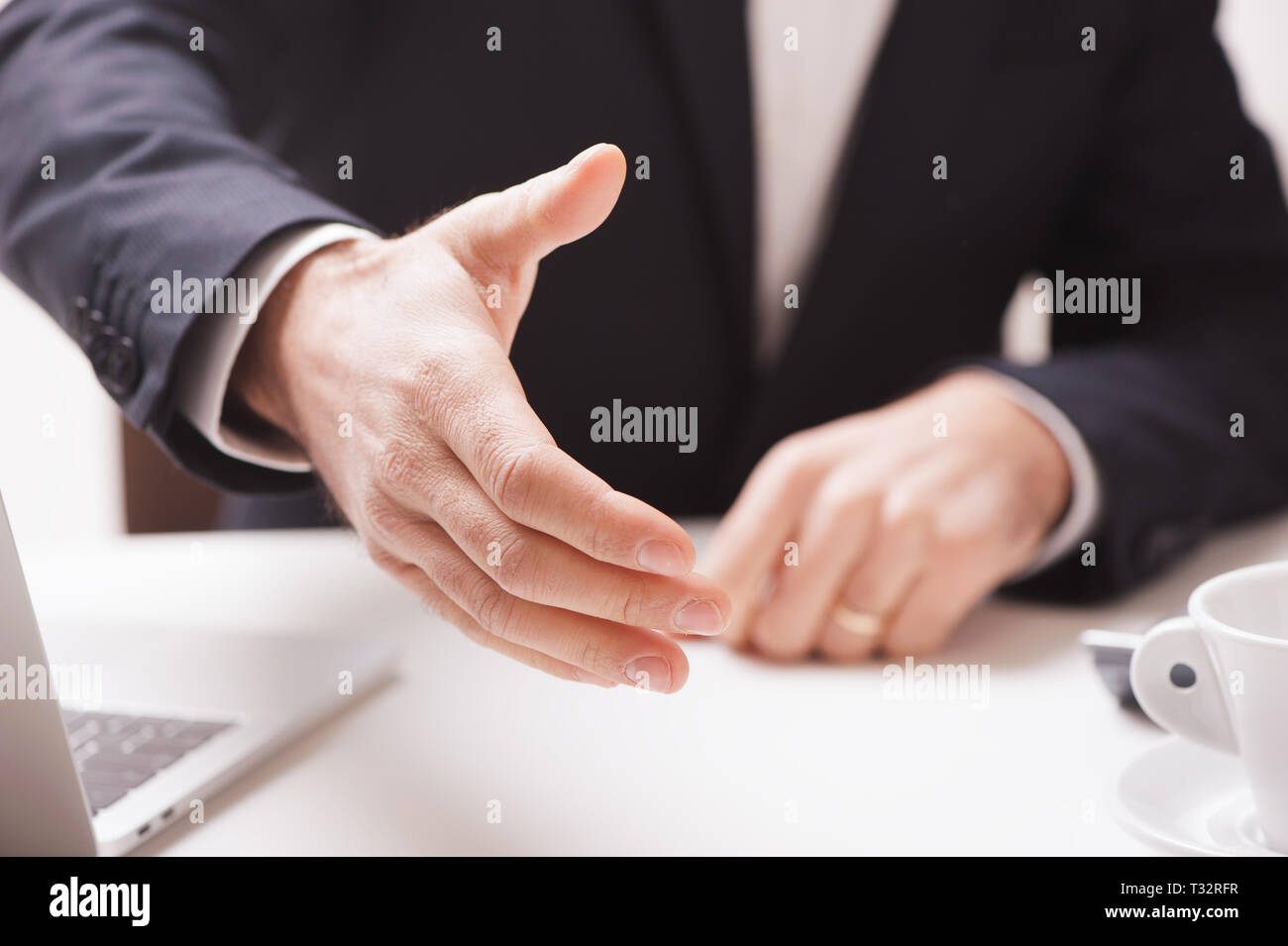Businessman offering a handshake sitting on his desk Stock Photo - Alamy
