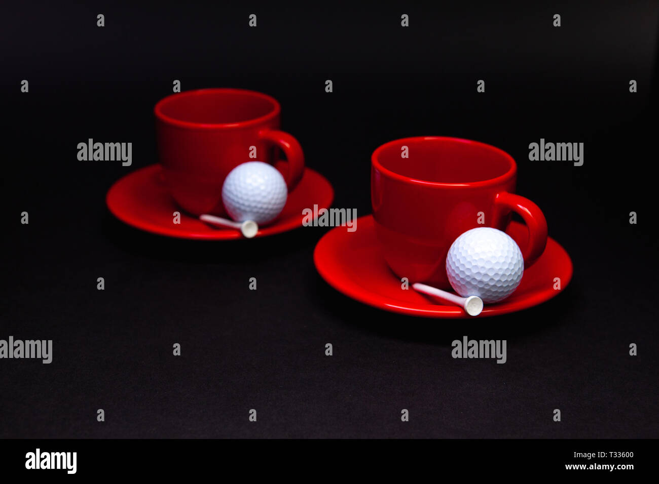 White golf balls and red cups of tea on the black table. Breakfast ...