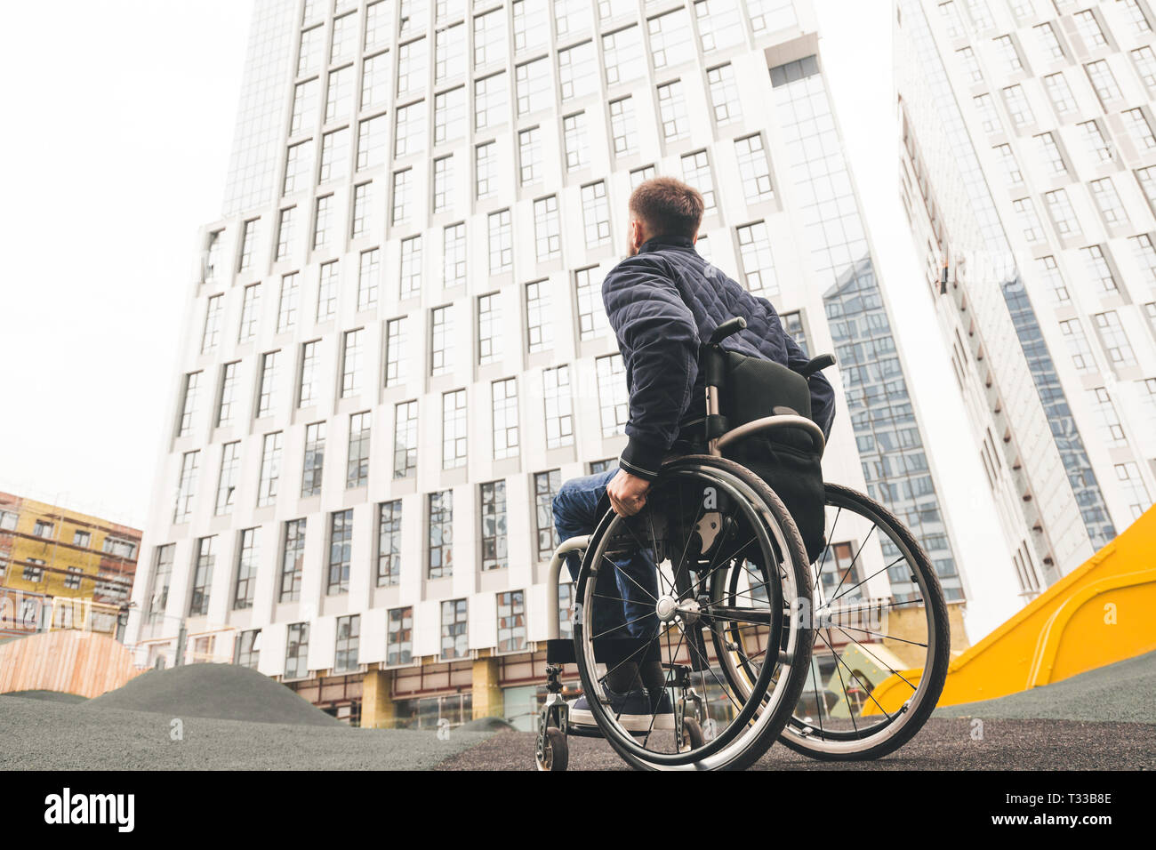 Young man in a wheelchair against the backdrop of a modern high-rise ...