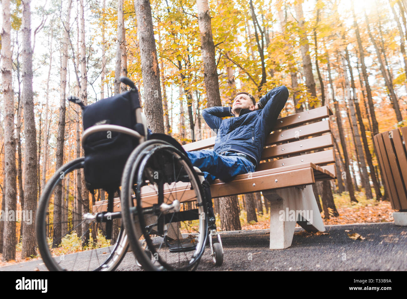 Young man resting sitting on a bench with his legs on his wheelchair ...