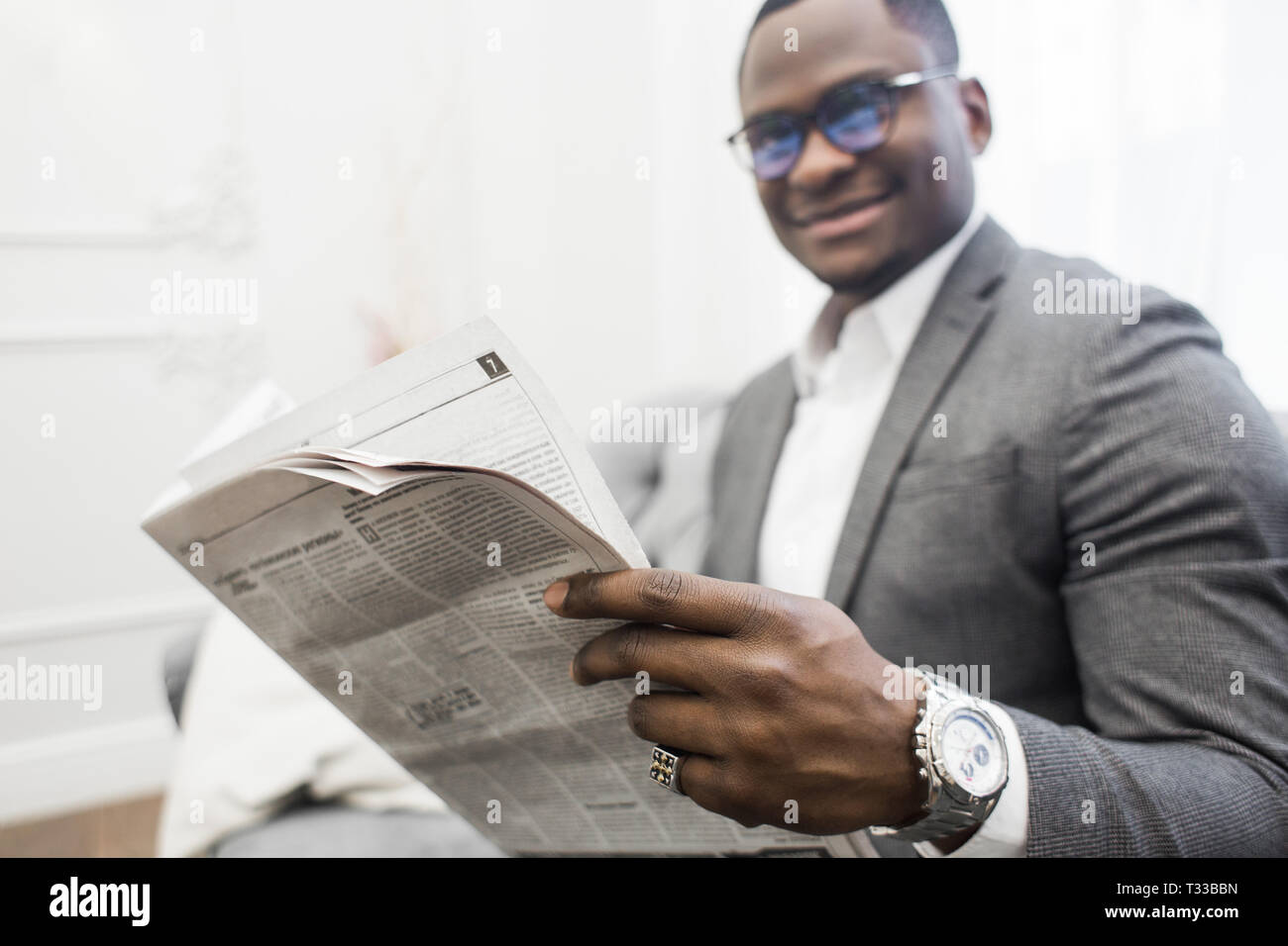 Young African American businessman in a gray suit reading a newspaper ...