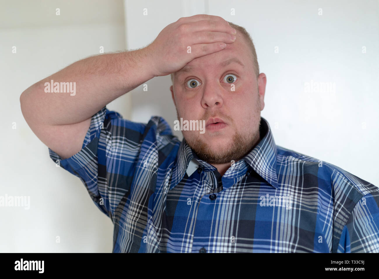 Shocked dazed young man in plaid shirt holding head with a hand Stock ...