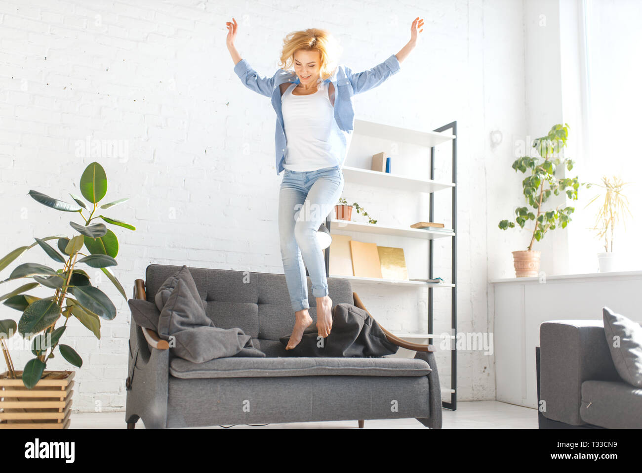 Young woman jumping on sofa hi-res stock photography and images - Alamy